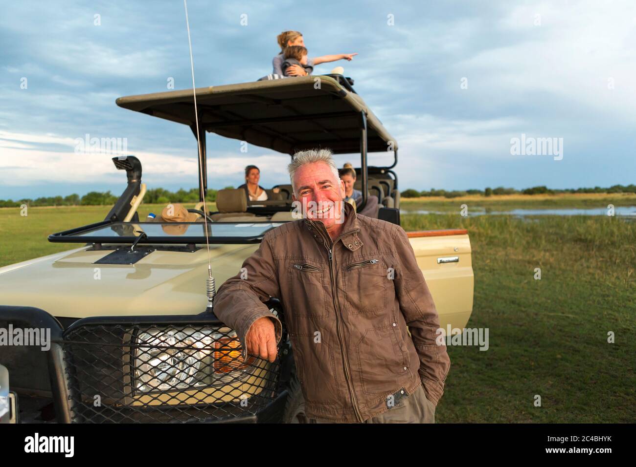 A smiling safari guide and family of tourists in a safari vehicle Stock ...