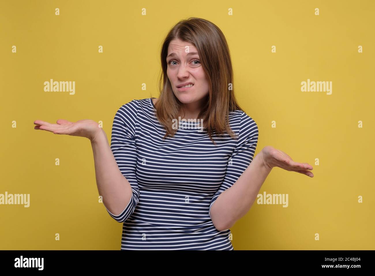 Attractive young woman shrugging her shoulders on yellow wall Stock ...