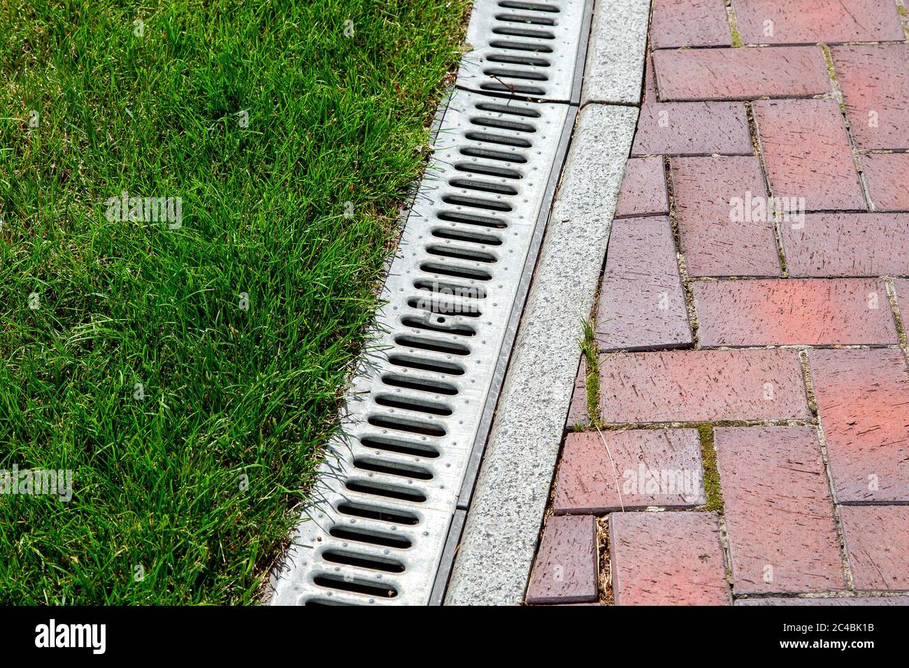 iron drainage system between paving slabs and green lawn, closeup of an ...