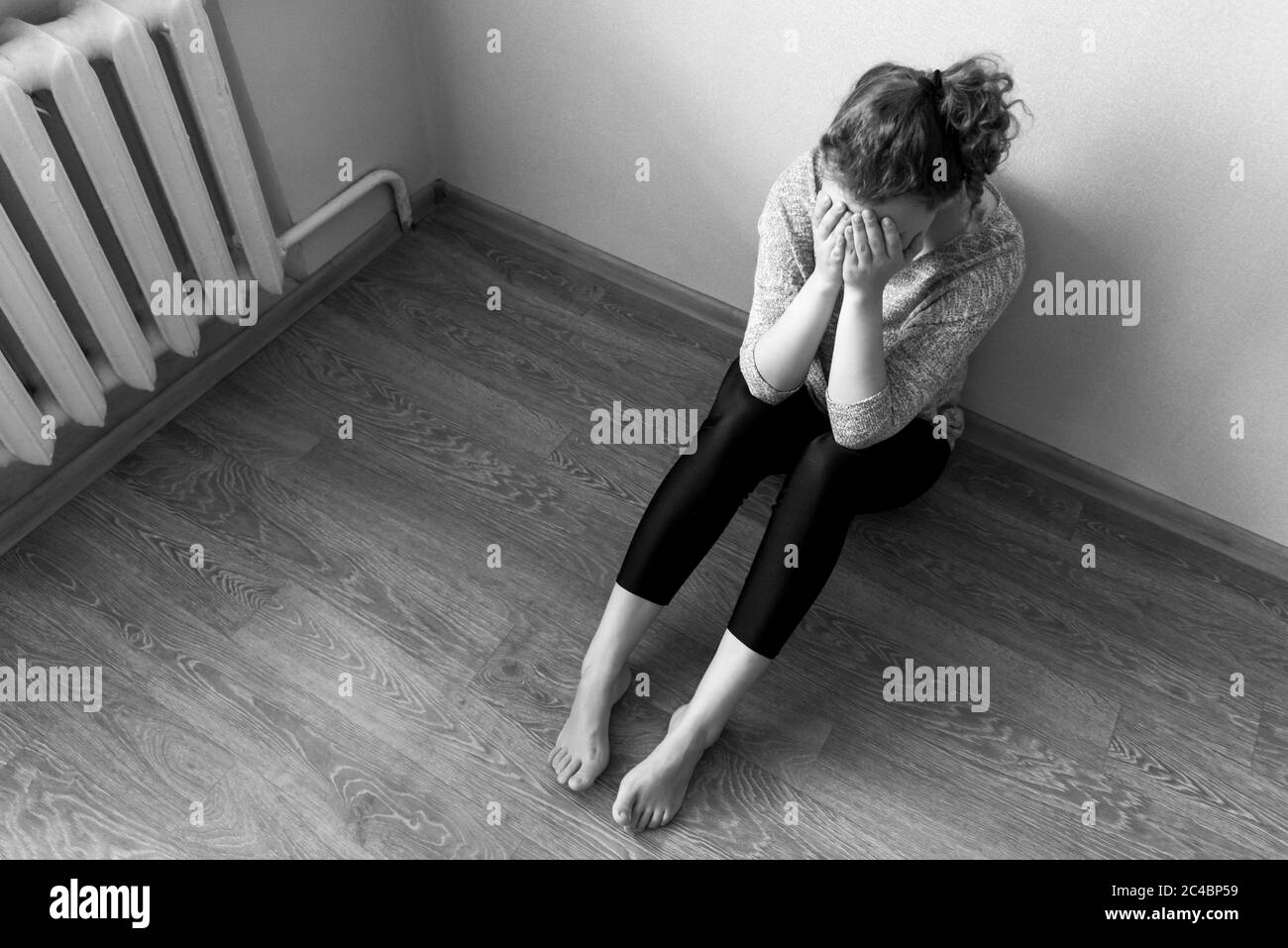 The girl is sitting on the floor and crying covering her face with her ...