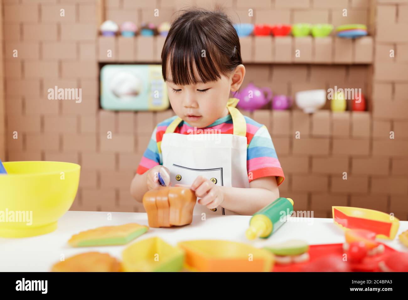 toddler girl pretend play food preparing role against cardboard blocks ...