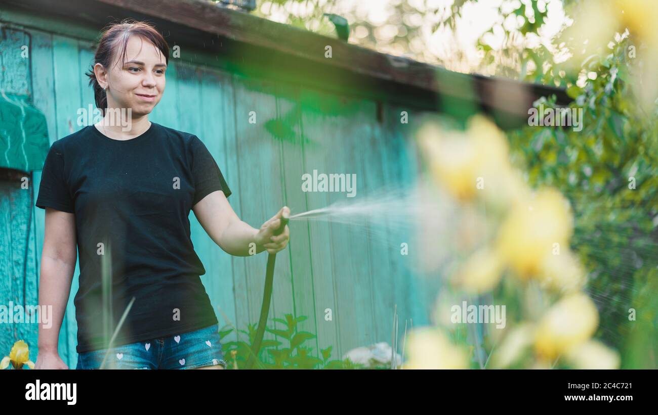 Young woman watering vegetable garden from hose. Close up of female ...