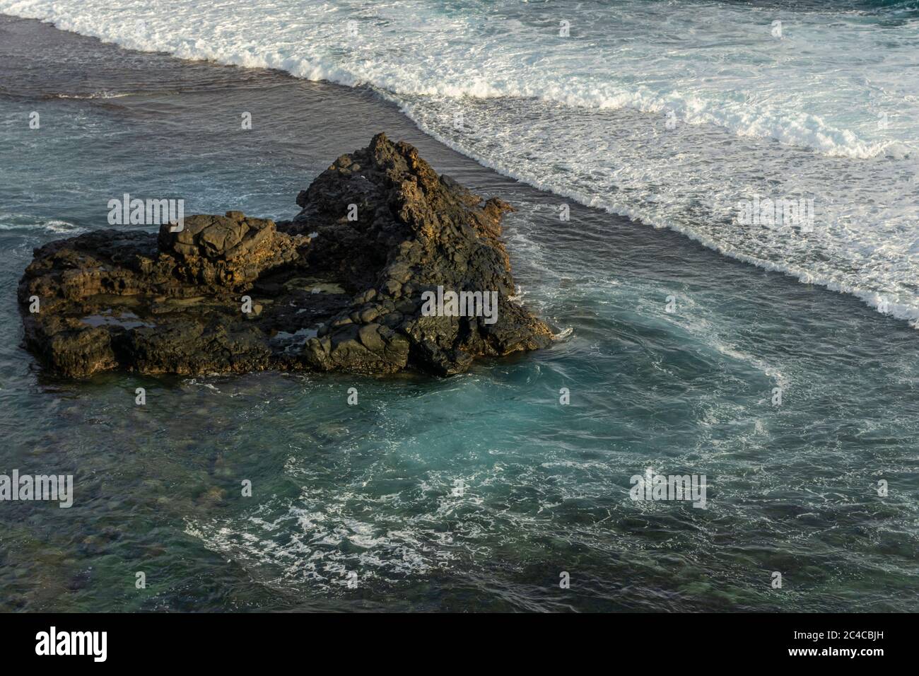 Big rock in the sea and foamy waves with spray running towards it Stock ...