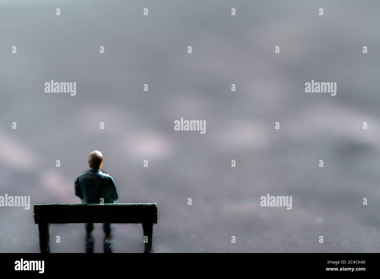 Miniature figurine posed as man sitting alone on a bench in surreal ...
