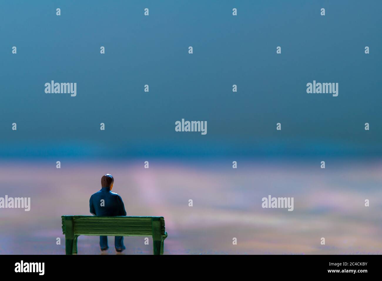Miniature figurine posed as man sitting alone on a bench in surreal ...