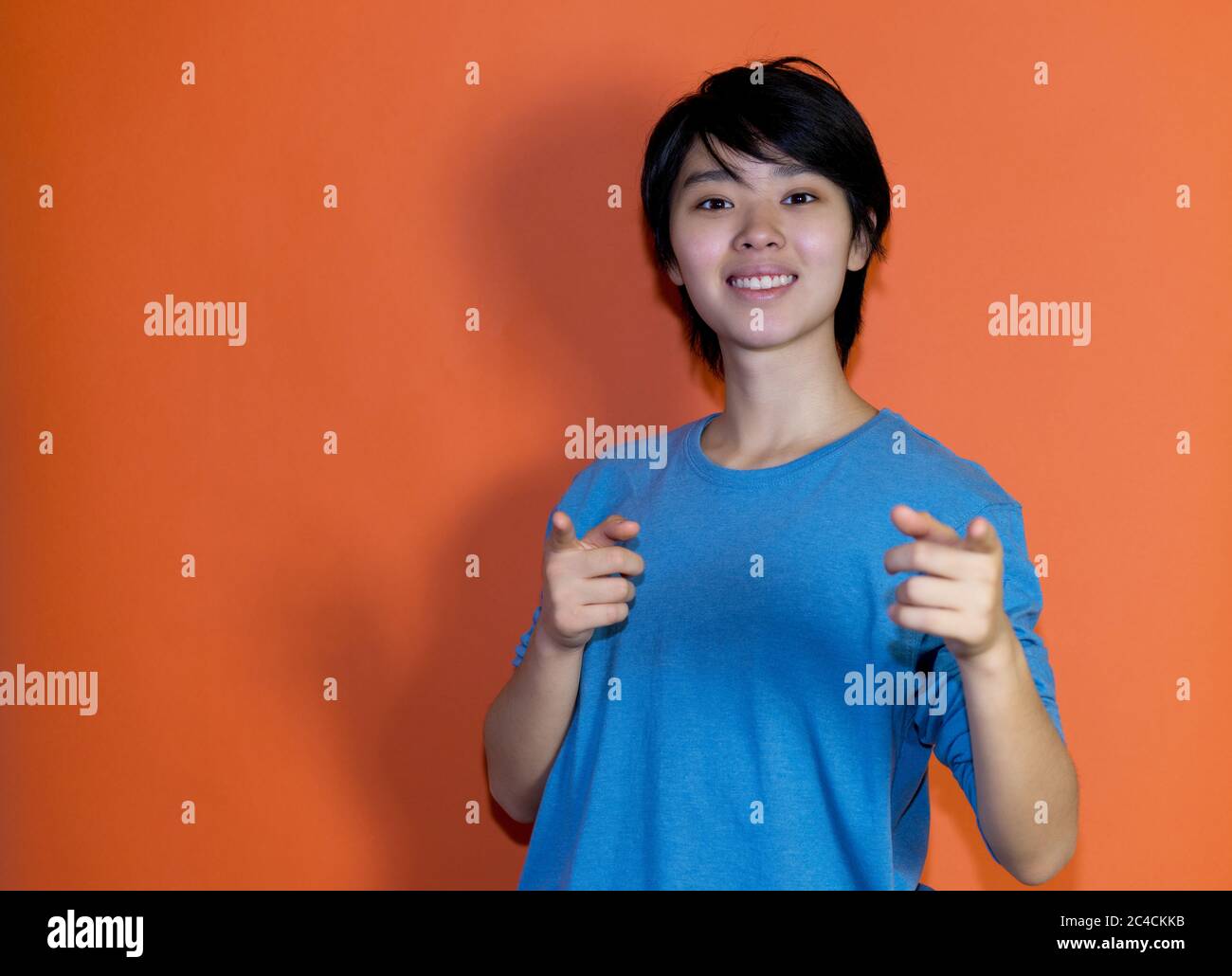Pointing chinese young adult man with blue shirt isolated on orange ...