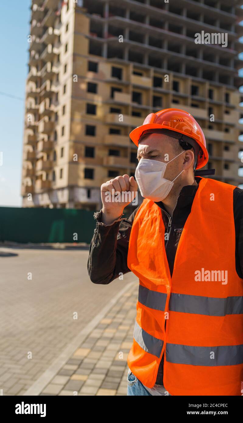 Male construction worker in overalls and medical mask coughing on ...