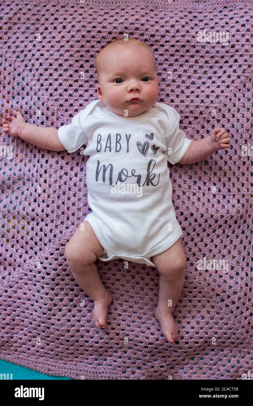 A newborn happy baby boy laying on a purple rug with a baby vest with ...