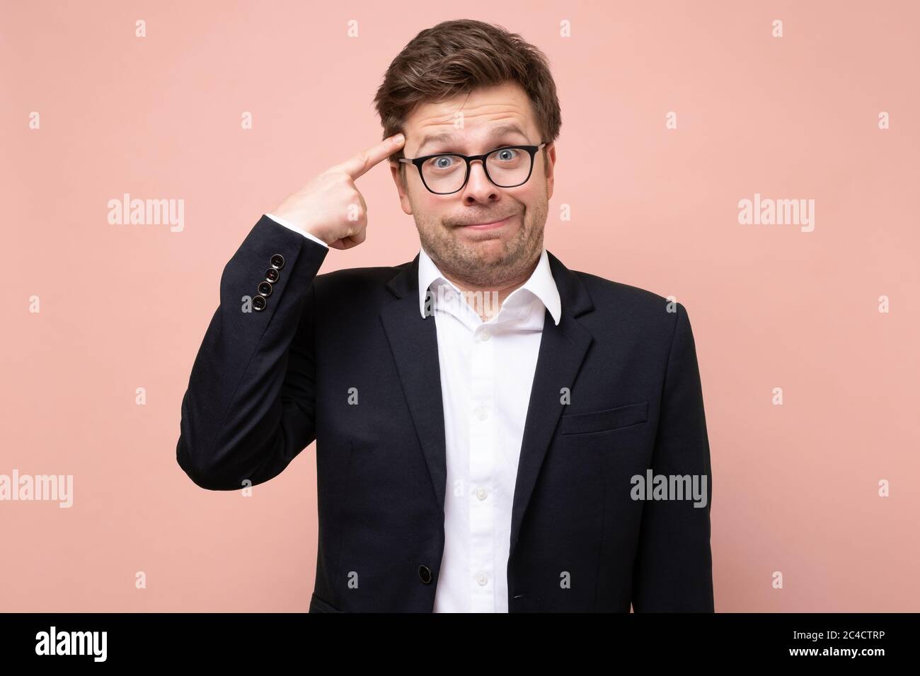 Confused young man gesturing with his finger against temple Stock Photo ...