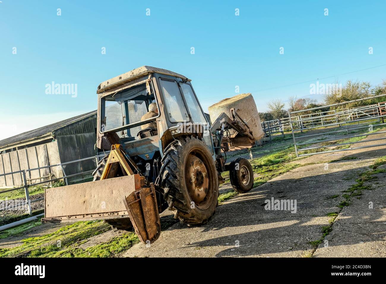 Farm tractor seen progressing between a straw barn and outbuilding, on ...