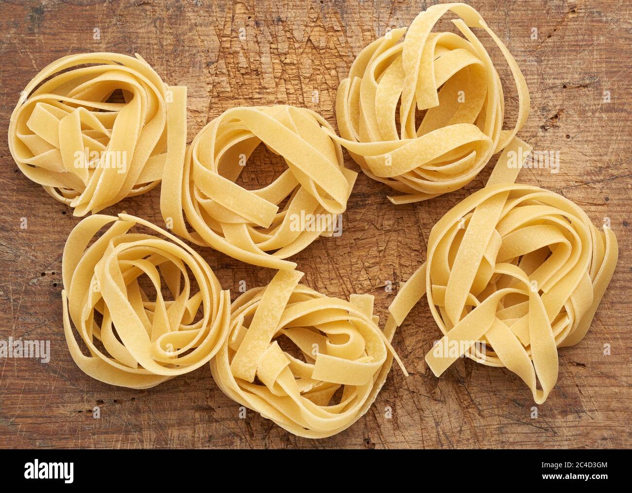 raw twisted pasta in round fettuccine nests, brown wooden background ...