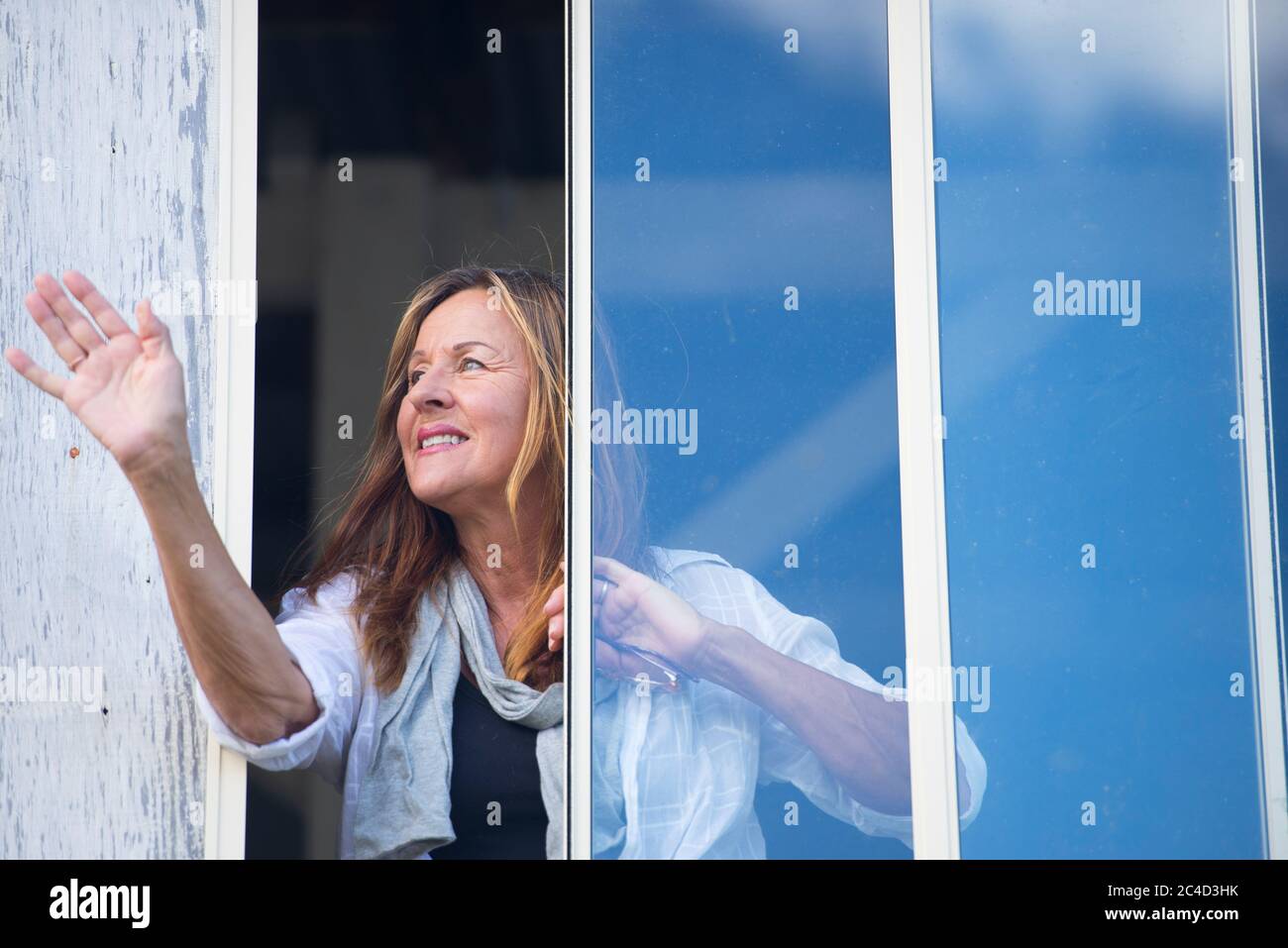 Portrait attractive mature woman standing at window waving happy ...