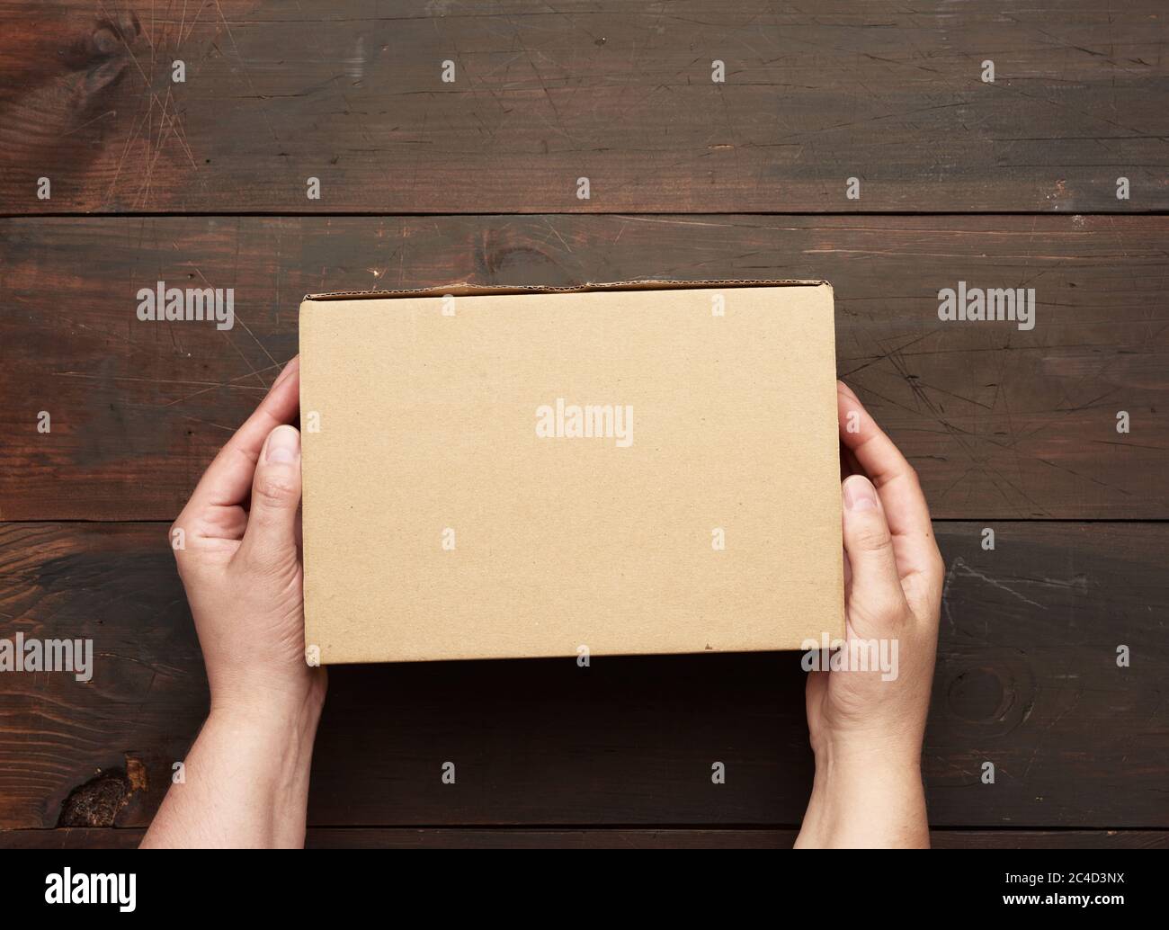 two hands holding a rectangular cardboard box of brown kraft paper over ...