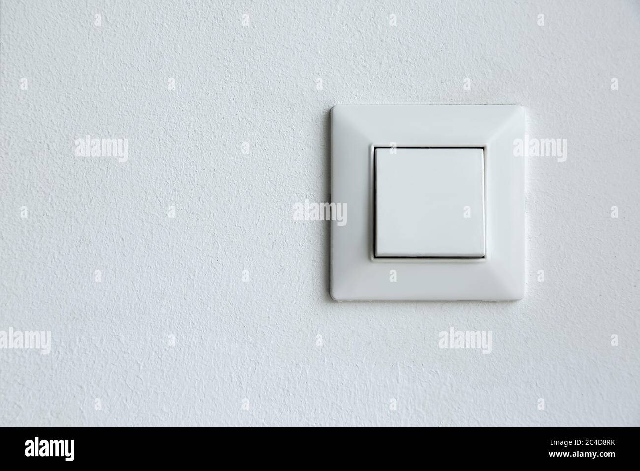 a square shaped white plastic light switch mounted on a white textured ...