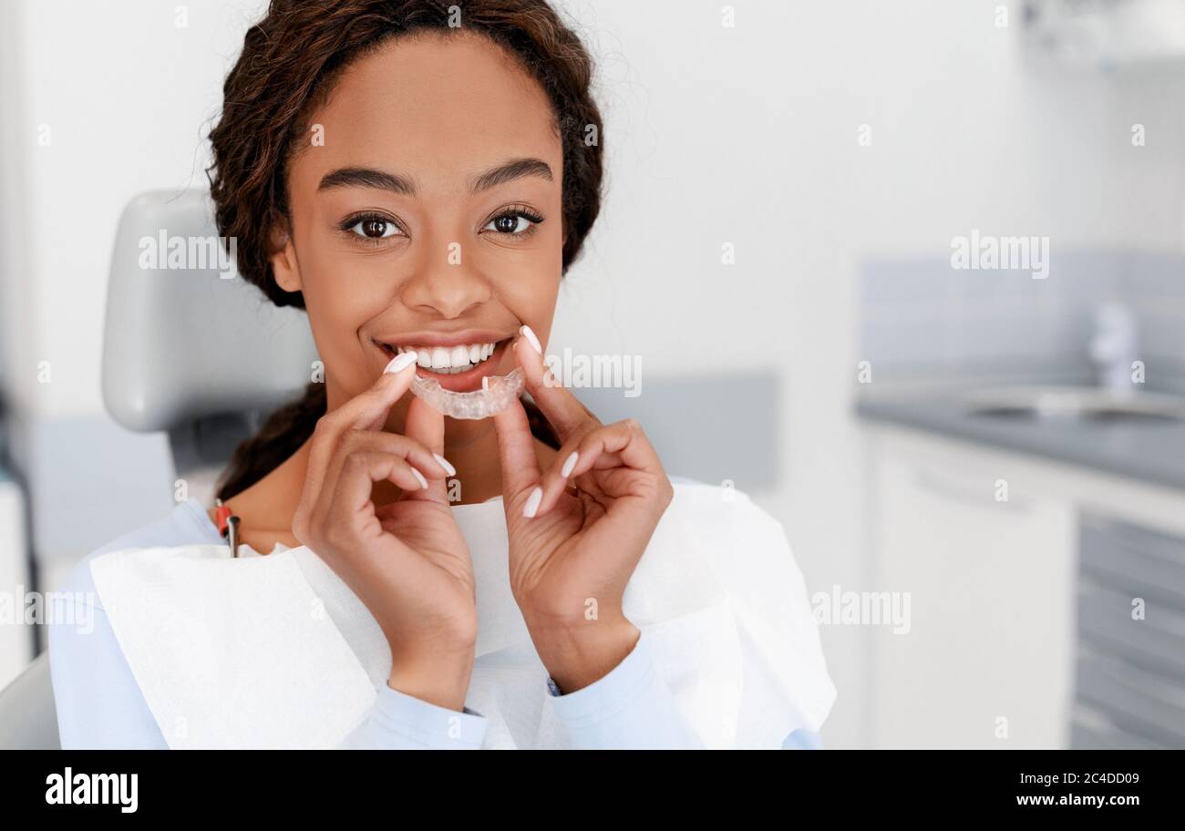 Smiling black girl holding invisible aligner, modern teeth trainer ...