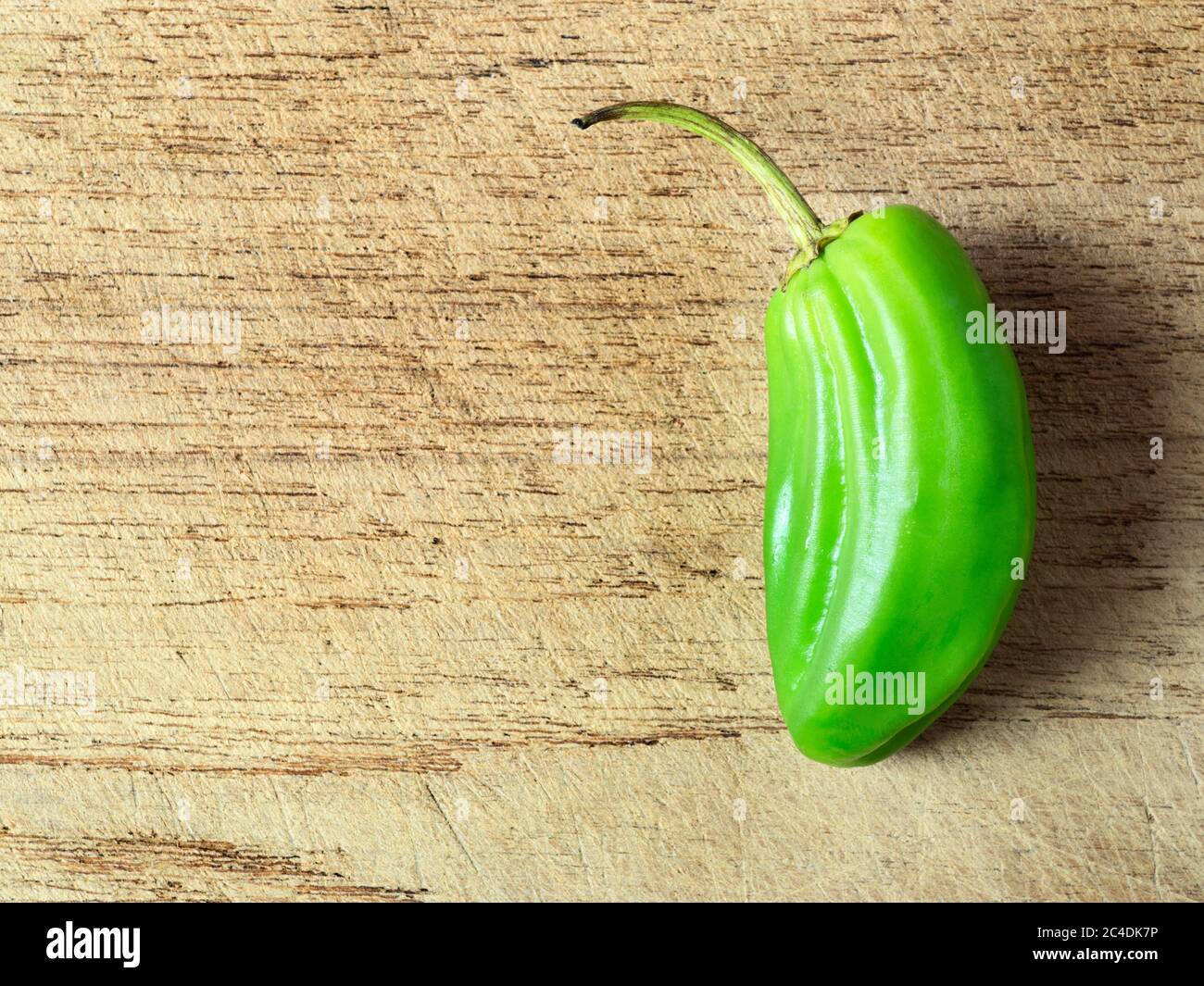 A single fresh green chilli pepper on a wooden chopping board with copy ...