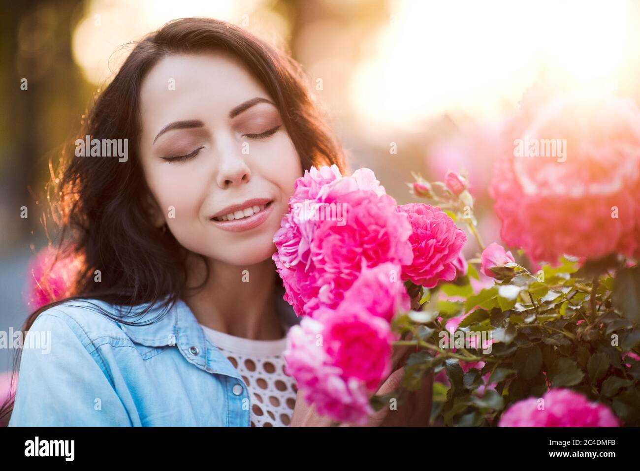 Smiling woman 24-25 year old smelling roses outdoors closeup. Summer ...