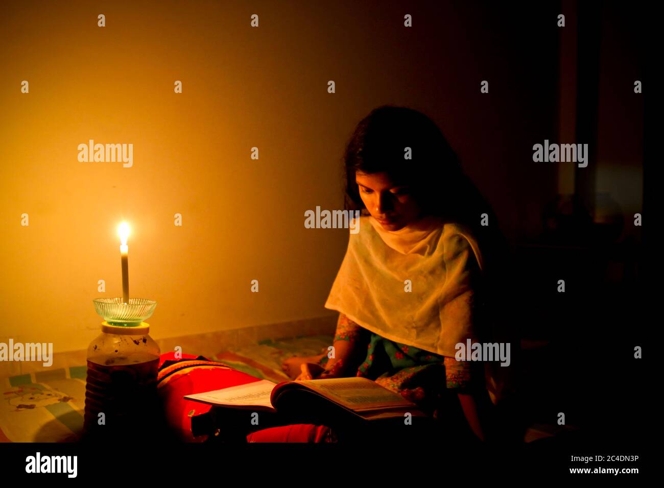 A young girl studying at home with candlelight after electricity load ...