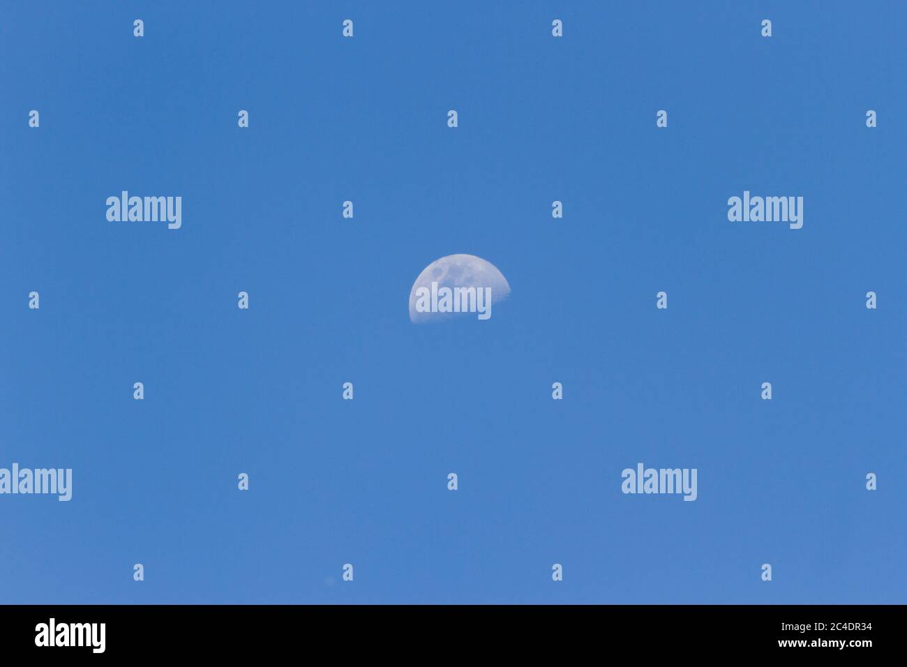Horizontal shot of a half-moon visible during daylight in the blue sky ...