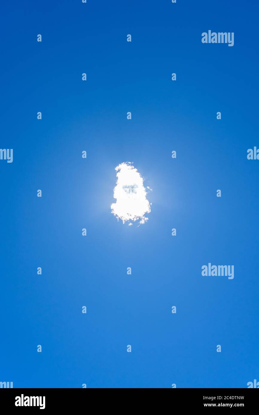 Cloud directly covering the sun and sunlight in a clean blue sky ...