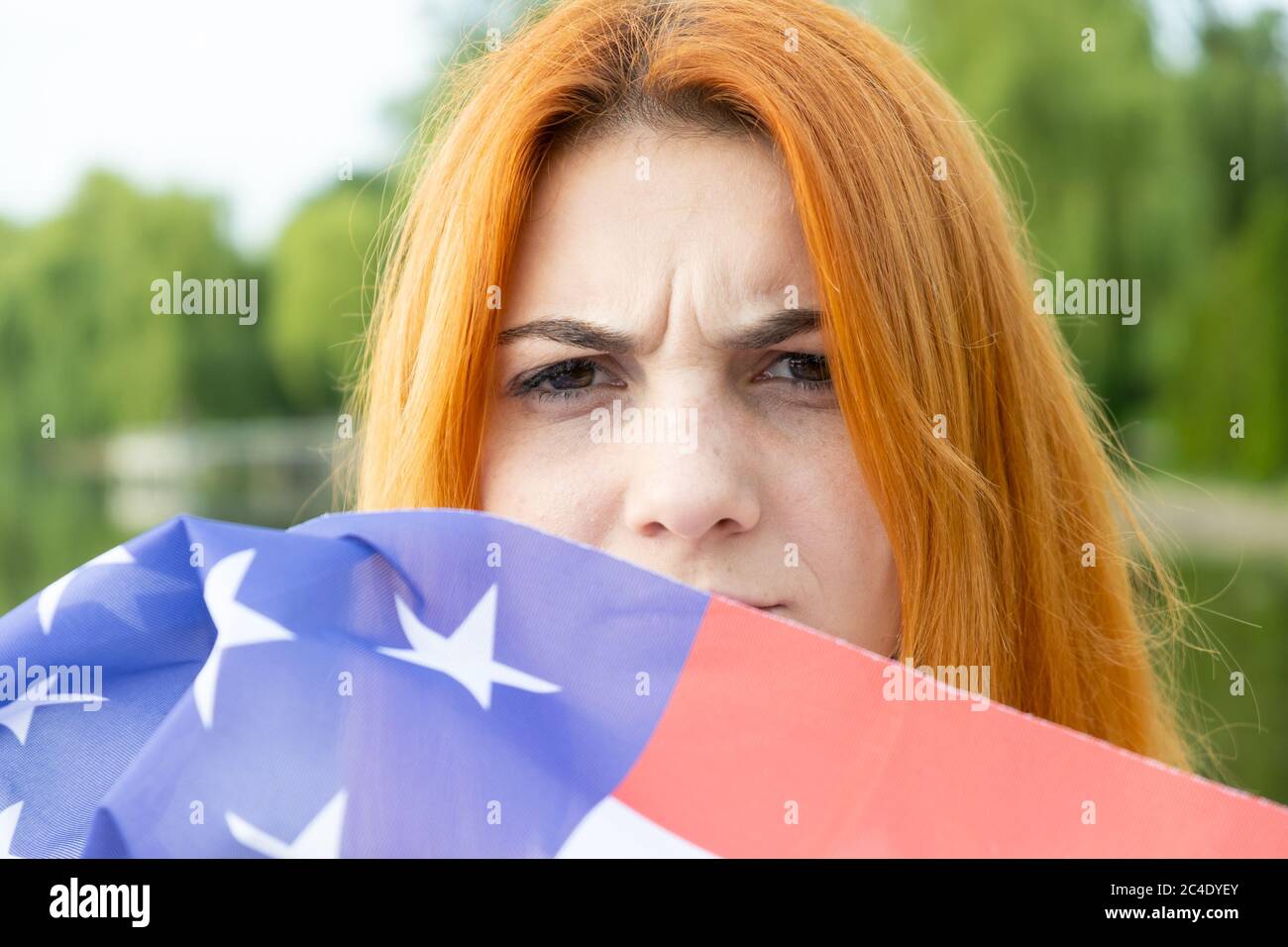 Portrait of angry red haired girl hiding her face behind USA national ...