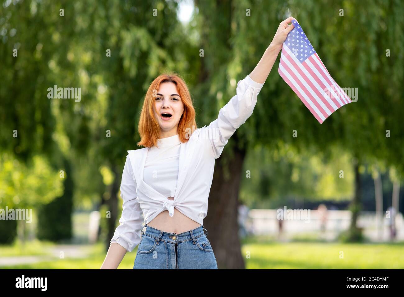 Angry young red haired woman protester posing with USA national flag in ...
