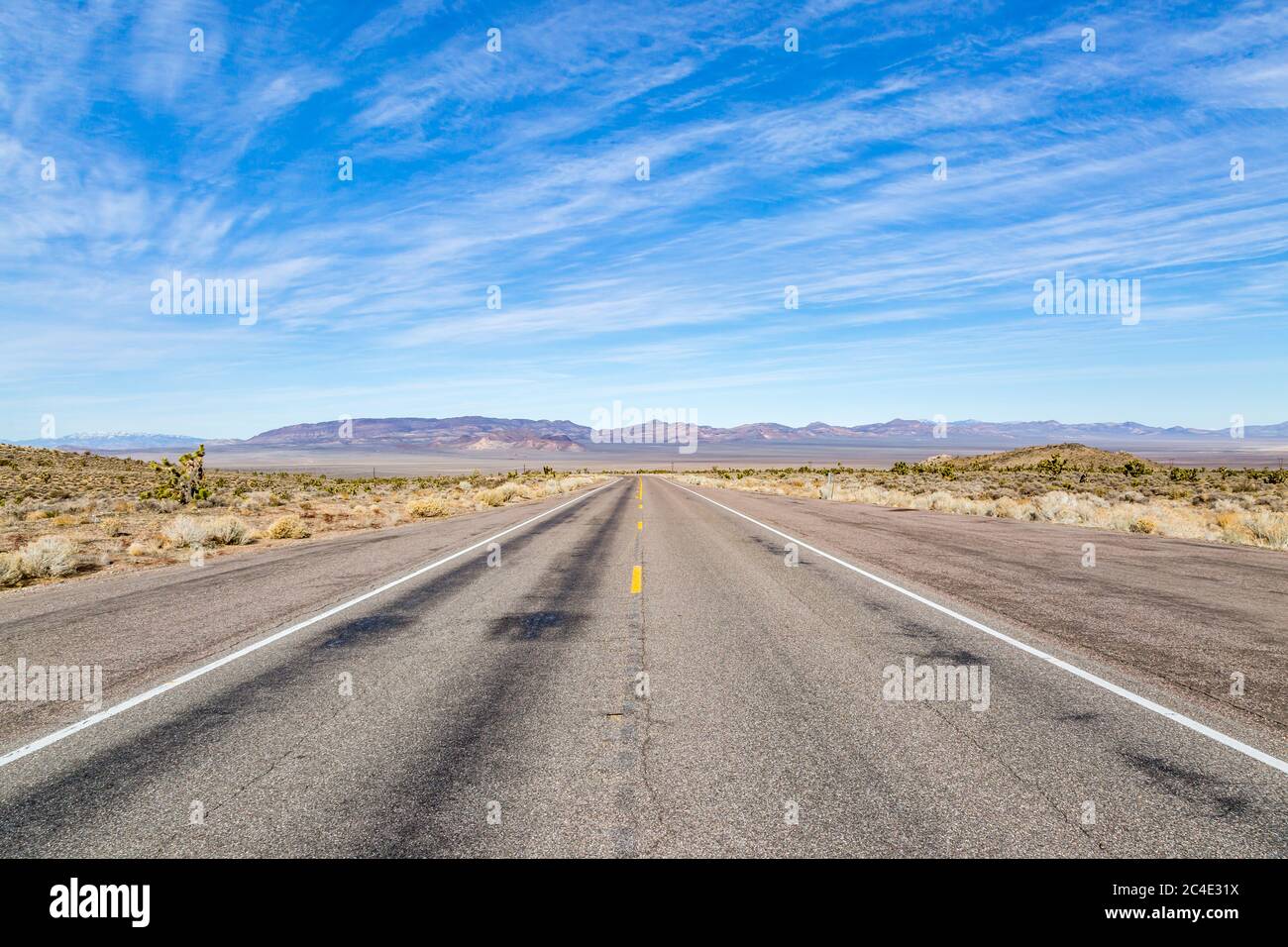 A long road through a remote Nevada landscape, with a blue sky overhead ...