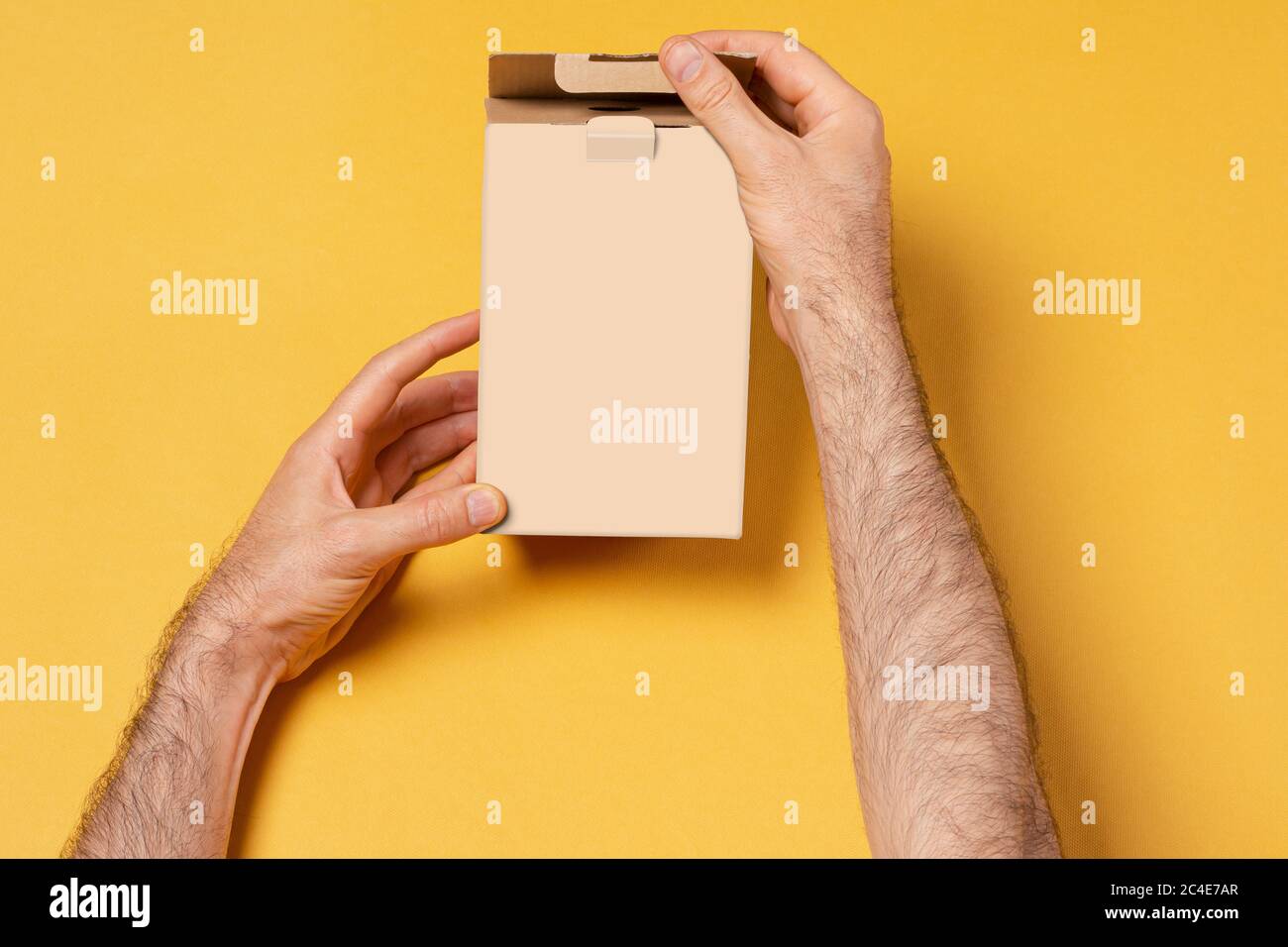 Male hand opening a small gift box in front of yellow background, mock ...