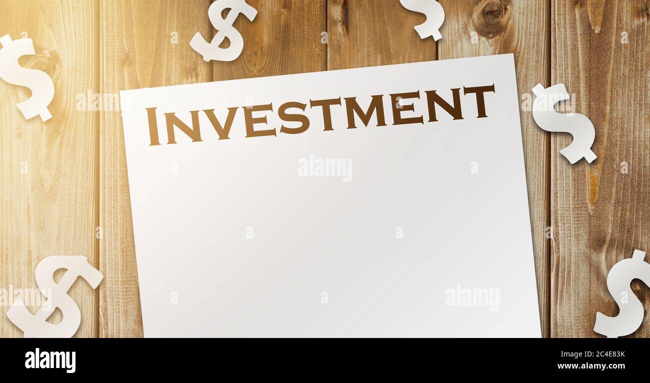 Investment word on page and paper dollar signs around on wooden table ...