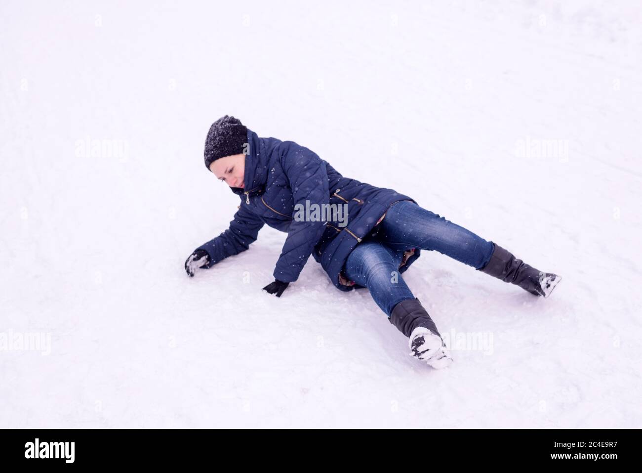 The girl slipped on ice covered with snow in the street, falling and ...