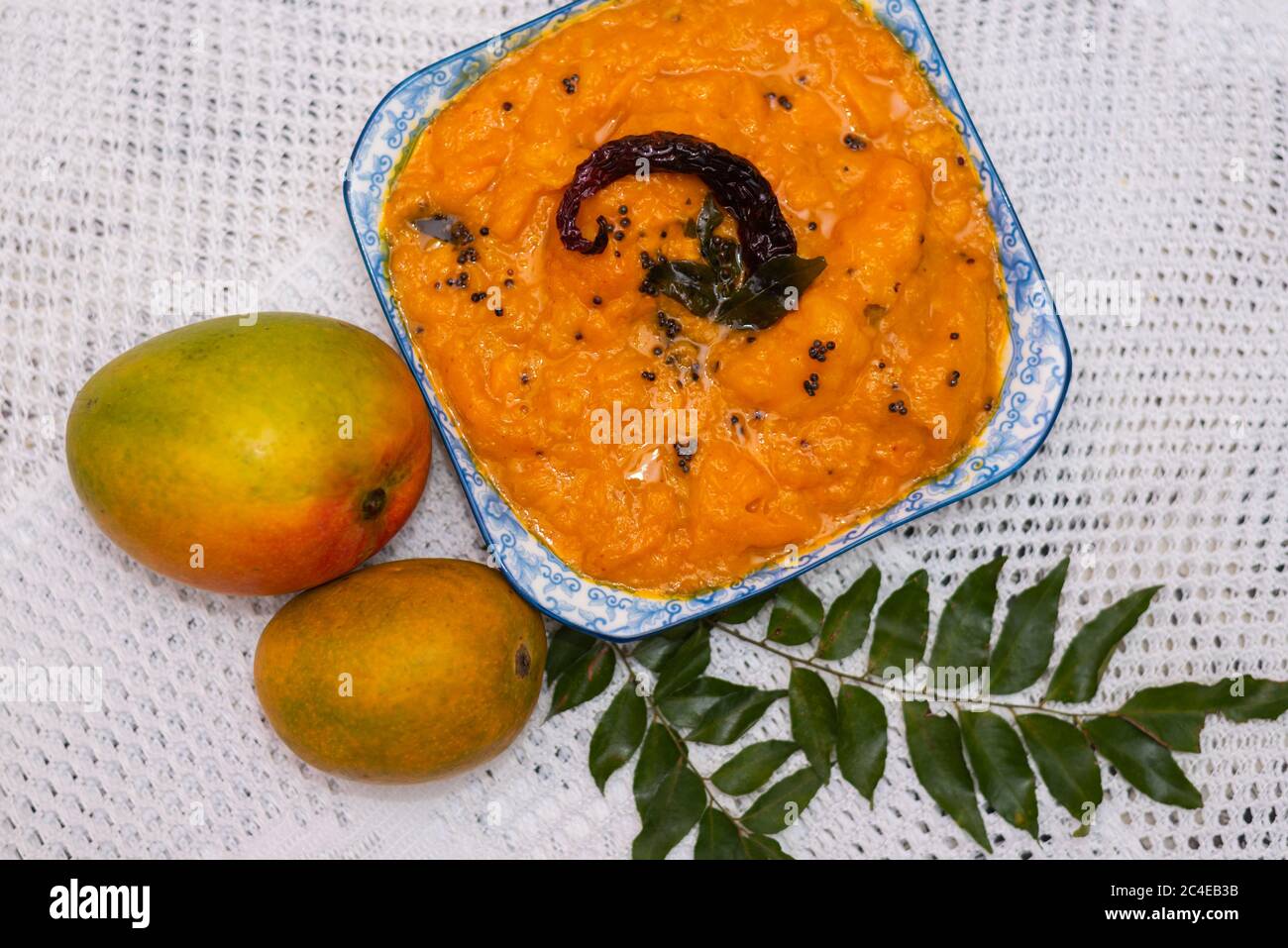Overhead shot of mango chutney on a plate surrounded by mango fruits ...