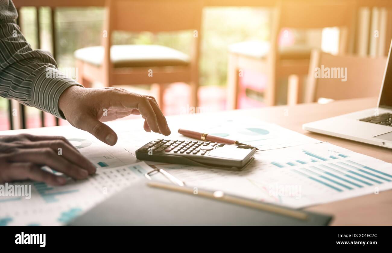 Businessman standing and using calculator about summary report on desk ...