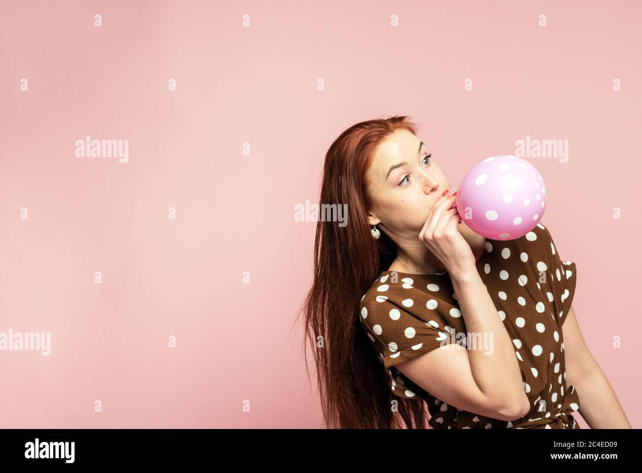 A girl with opened-eyes is blowing. A redhead girl is inflating the ...