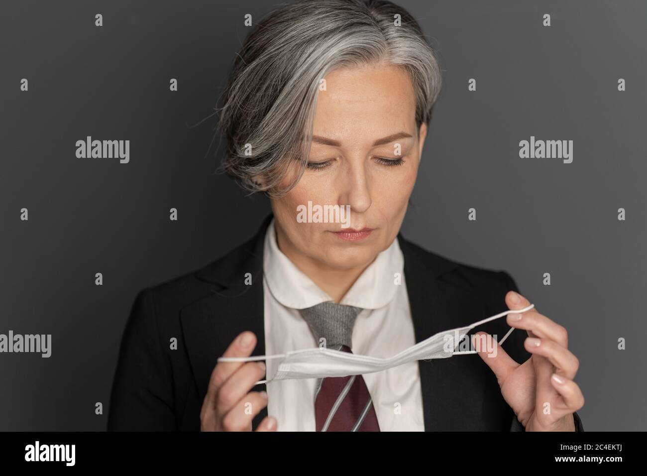 Pensive gray-haired business woman putting on a protective mask on her ...
