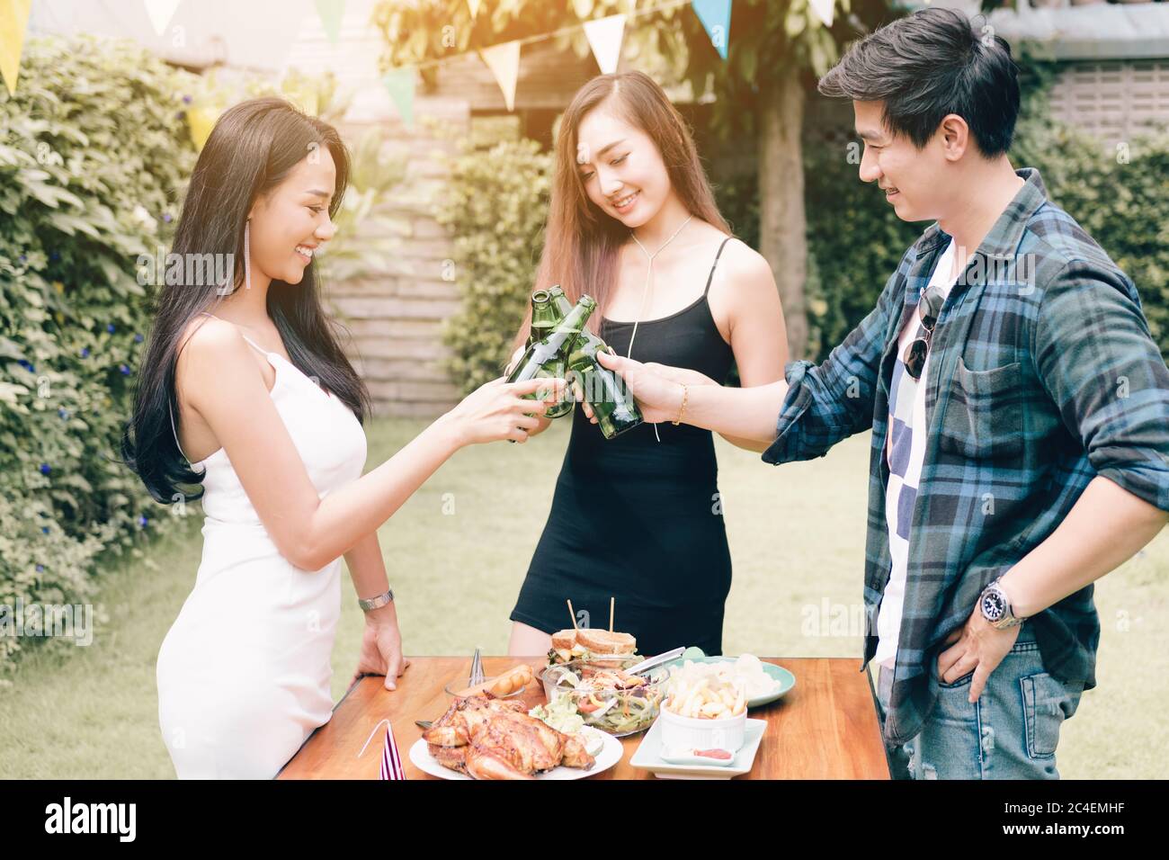 Asian group happy friends toasting with beer bottles at the garden home ...