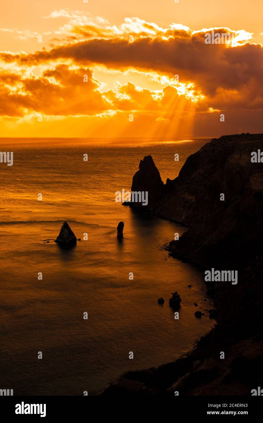 A red burning sunset with the silhouette of a cliff over the sea on ...