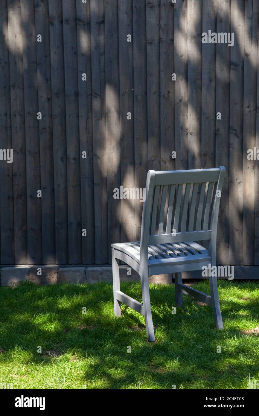 Grey garden chair, grey background, grey fence panel, shadows, grass ...