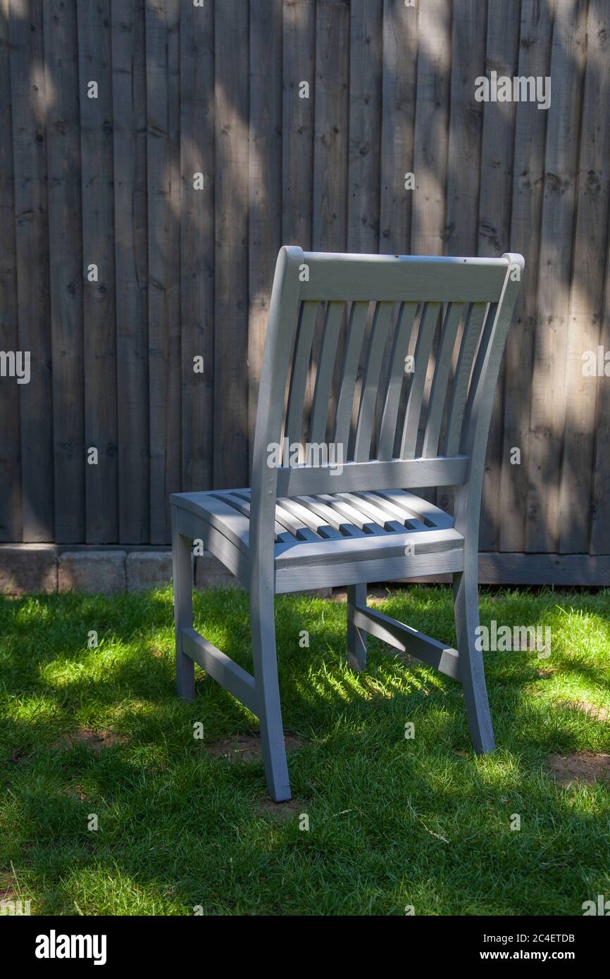 Grey garden chair, grey background, grey fence panel, shadows, grass ...