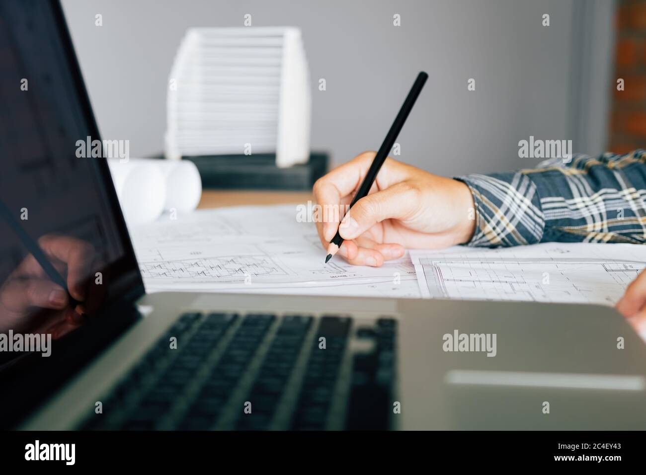 Hand of young engineering man drawing on blueprint with laptop on desk ...