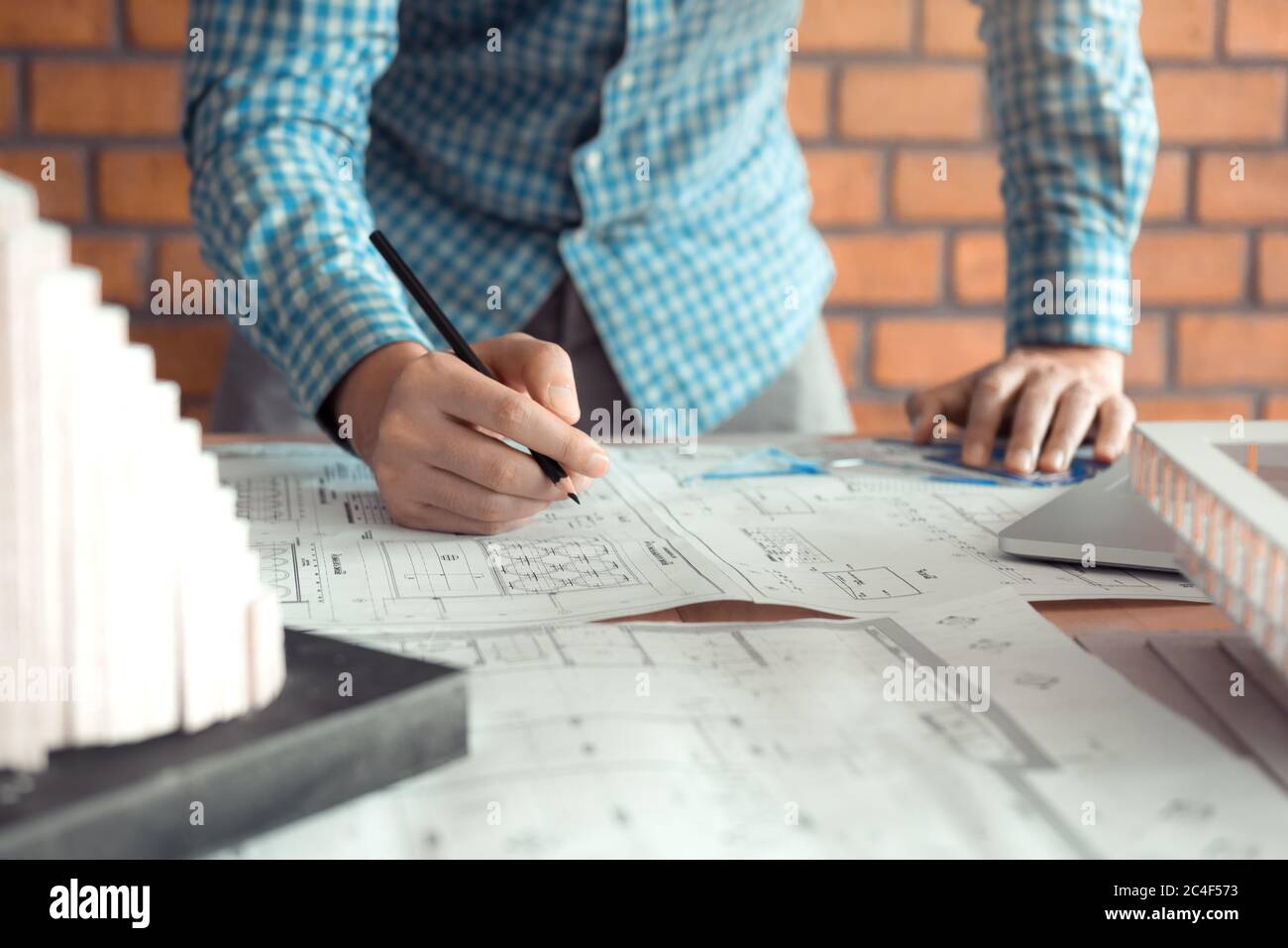 Hand of young engineering man drawing on blueprint with model on desk ...