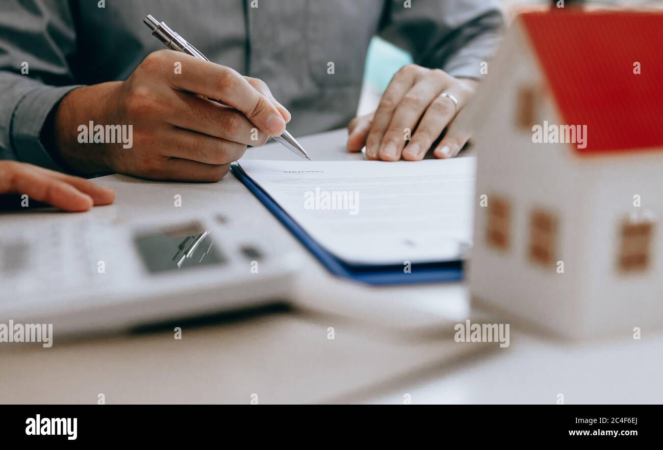 Asian man signing paper contract agreement for house with model home ...