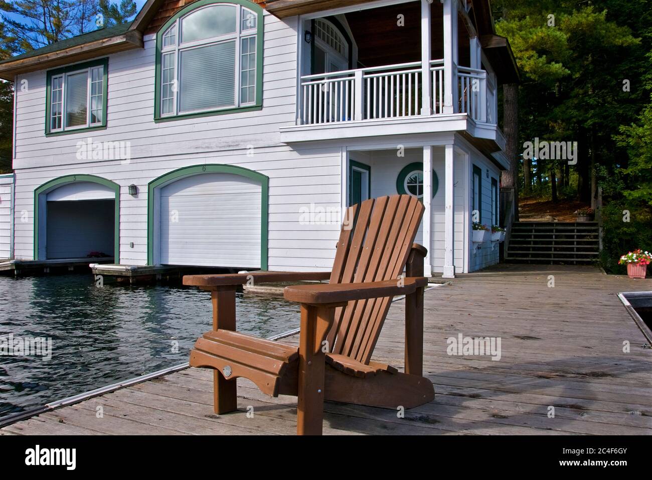 A Muskoka chair sitting on a wood dock facing a calm lake. Pier for ...