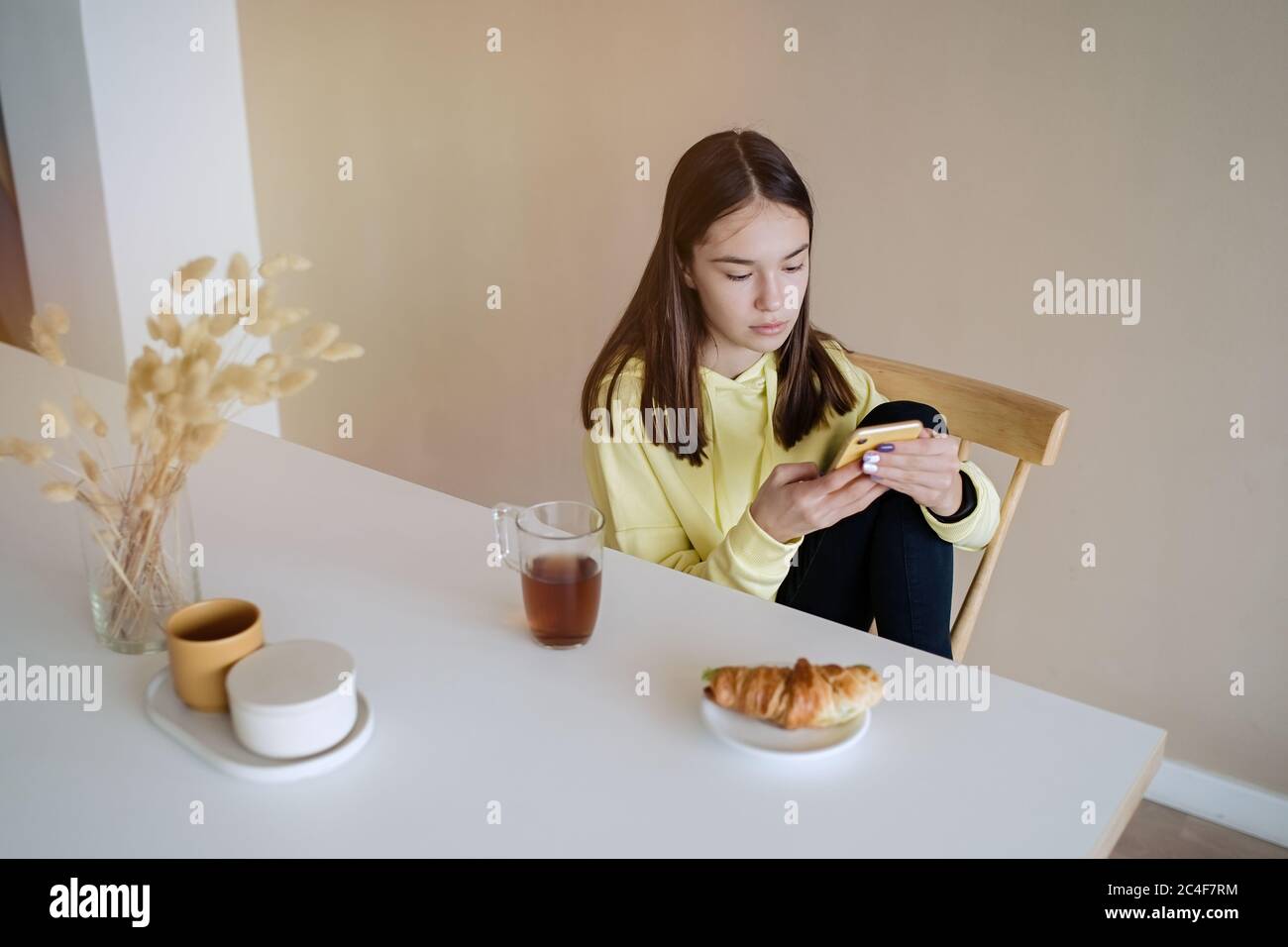 Cute teen girl eating breakfast in kitchen while using on her smart ...