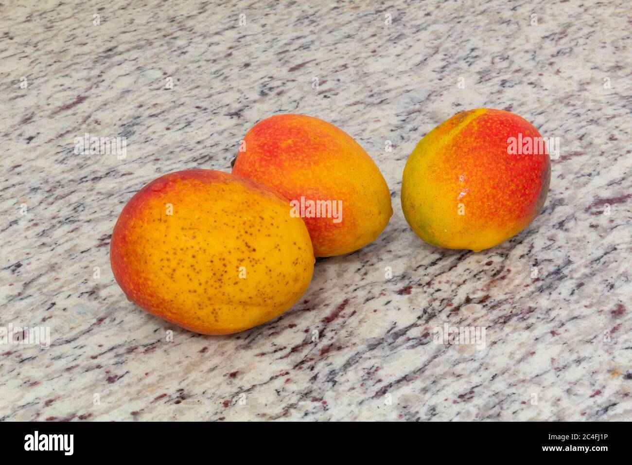 three colorful mangoes on a light colored background Stock Photo - Alamy