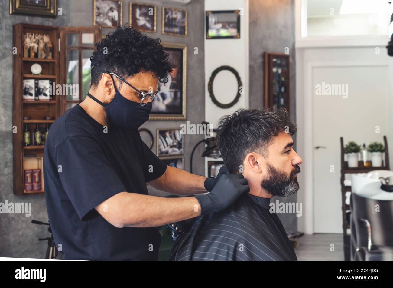 Mulatto barber putting neck cover paper in a barbershop. Client with ...