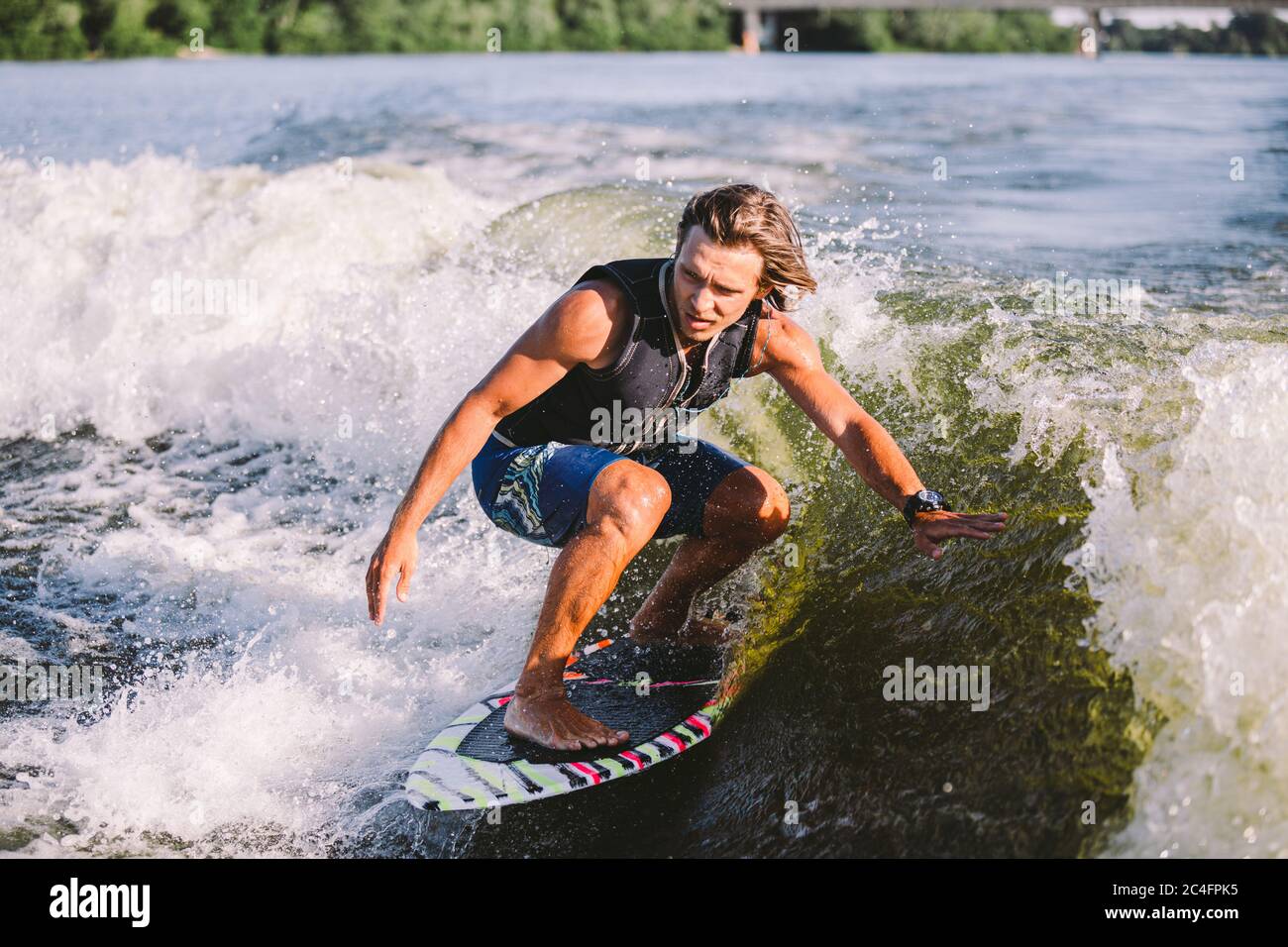 Active wakesurfer jumping on wake board down the river waves. Surfer on ...