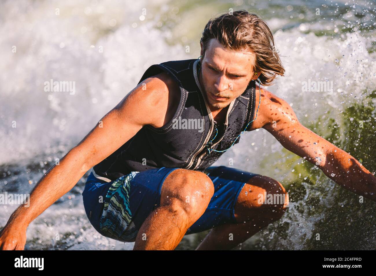 Active wakesurfer jumping on wake board down the river waves. Surfer on ...