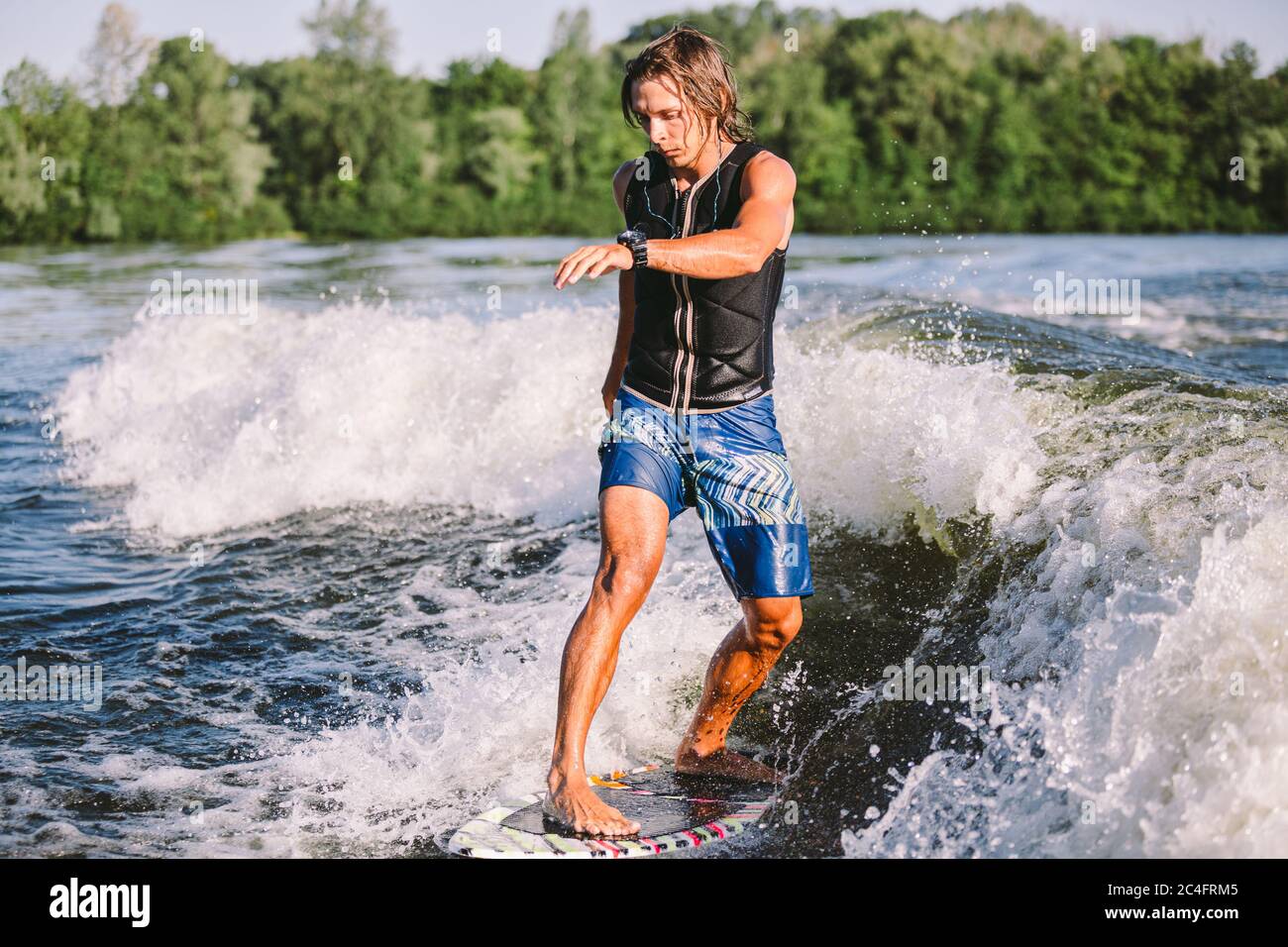 Beautiful long haired blond wakesurf in vest on board along waves of ...