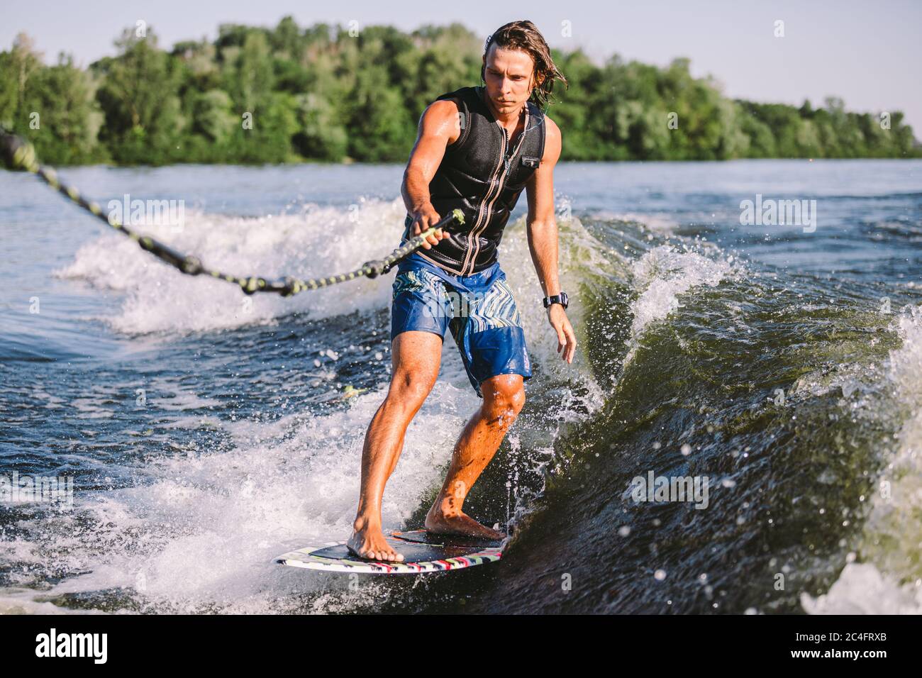 Beautiful long haired blond wakesurf in vest on board along waves of ...