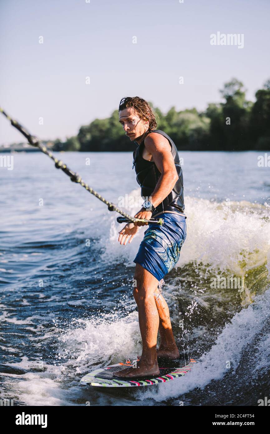 Active wakesurfer jumping on wake board down the river waves. Surfer on ...
